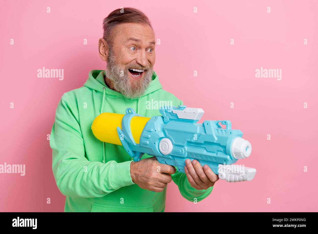 Photo of excited funky guy dressed green hoodie shooting water gun ...