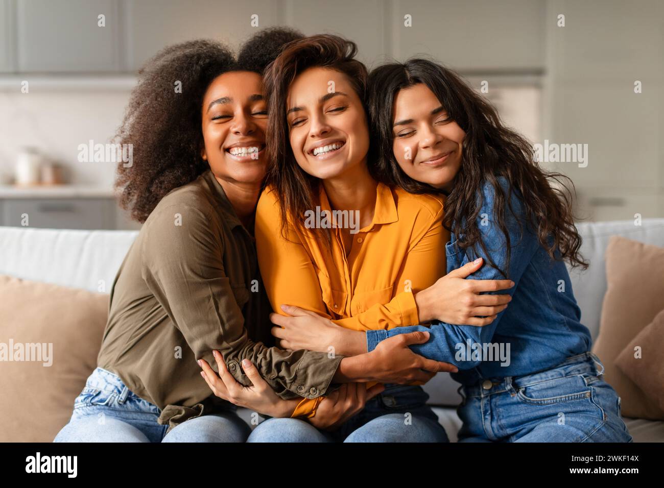 Three joyful young multiethnic women hugging and smiling together ...