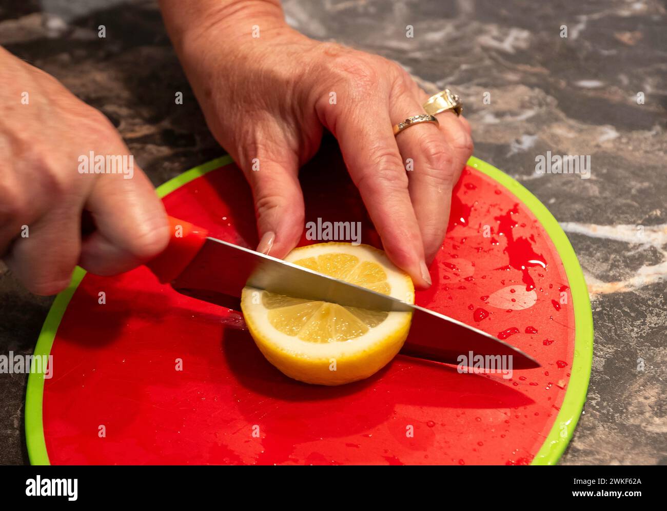 Womans hands dividing a yellow lemon slice in half while holding the ...