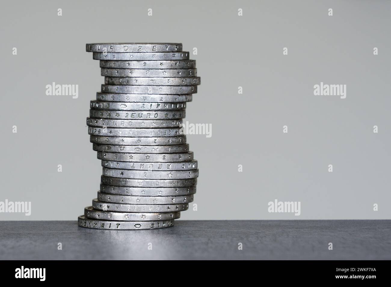 Vertical unstable curved pile of two euro coins on a grey background ...