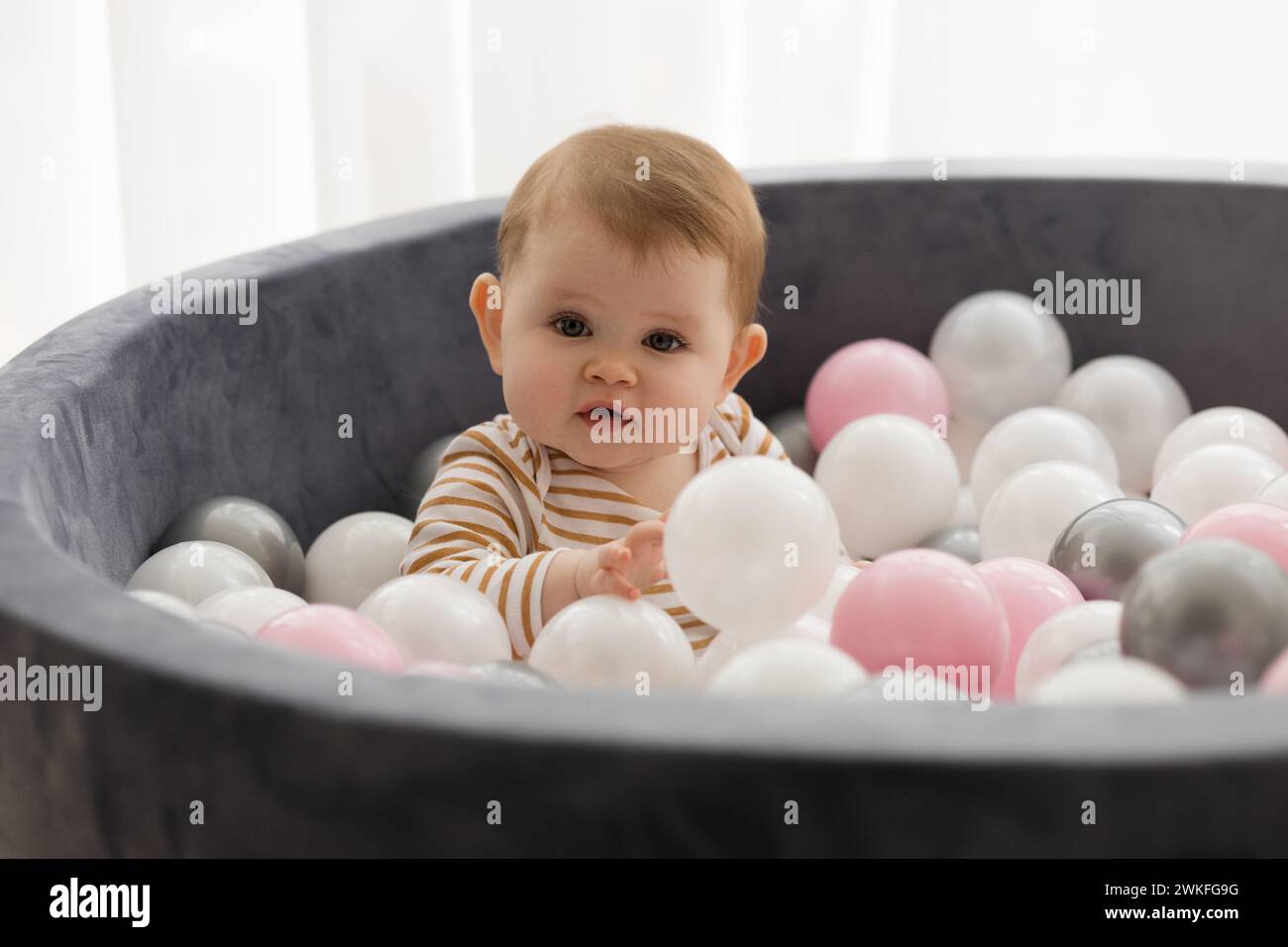 a baby is sitting in a ball pit holding a ball Stock Photo - Alamy