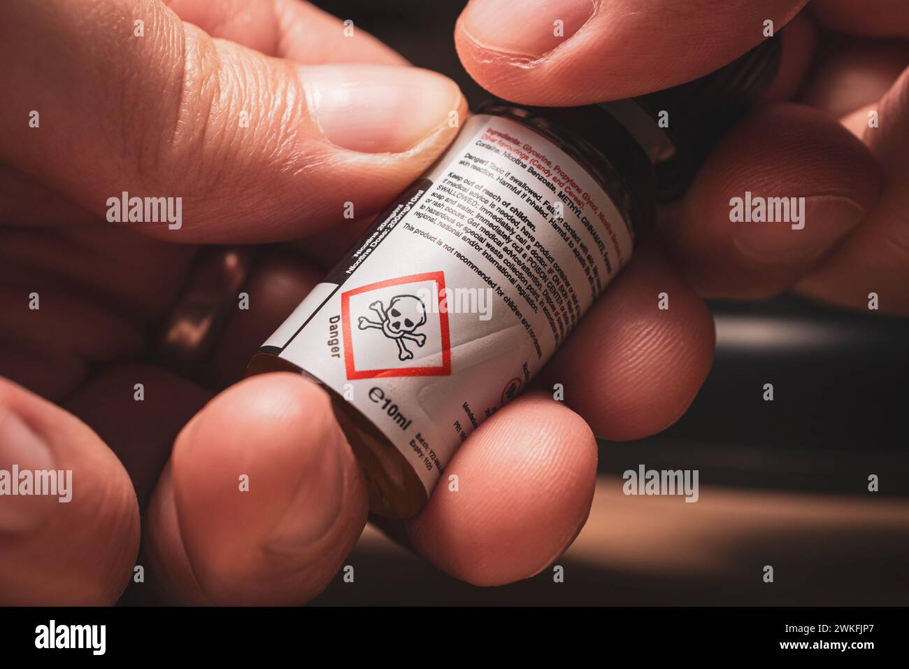 Hands holding an e-liquid bottle with a danger skull warning sign and ...