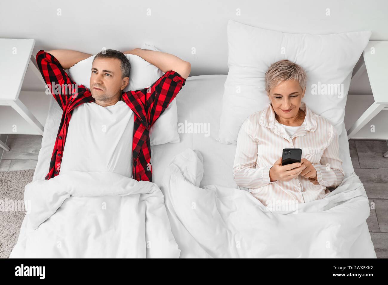 Offended mature man and his wife using mobile phone in bedroom Stock ...