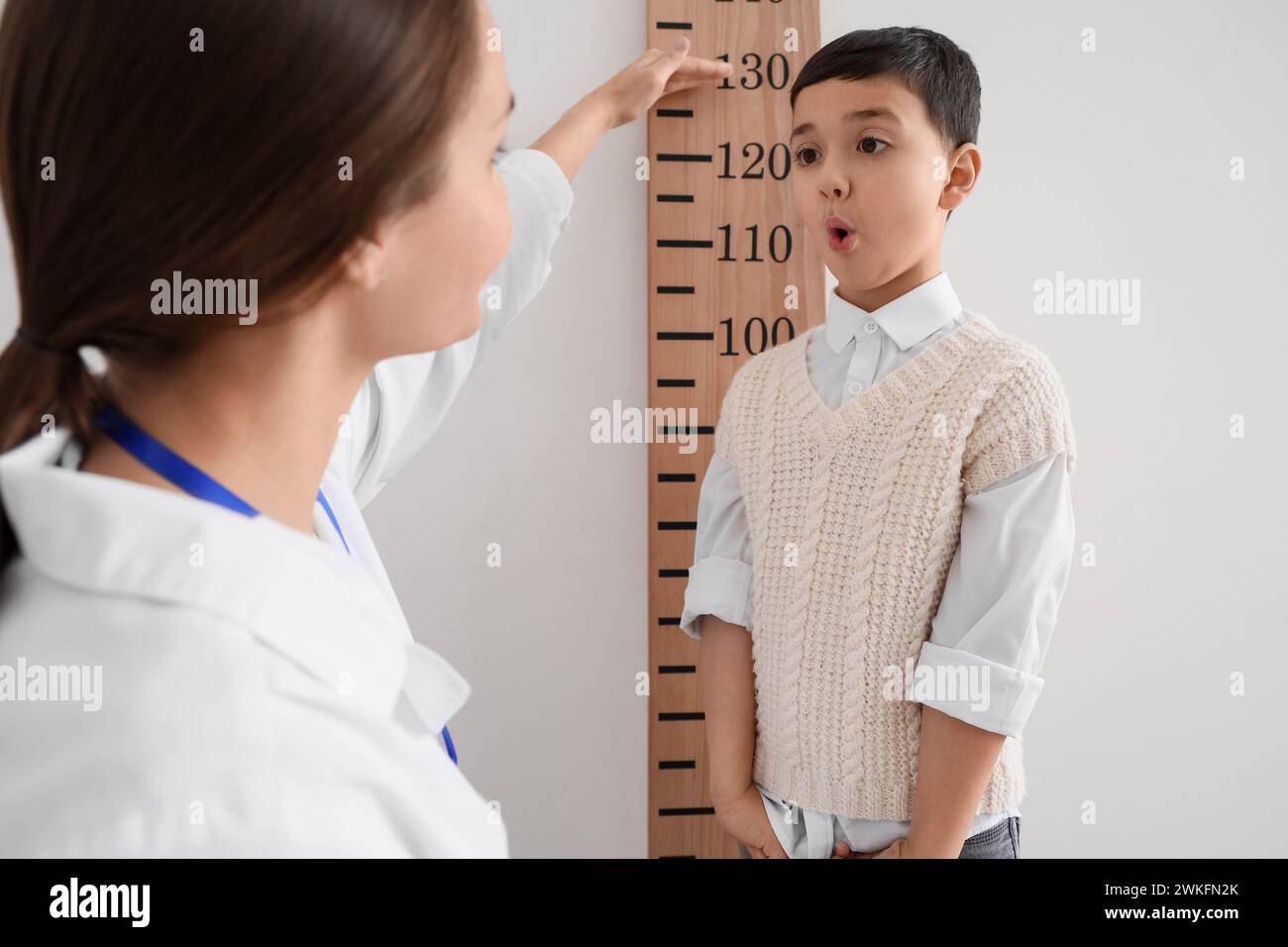 Pediatrician measuring height of surprised little boy near wooden ...