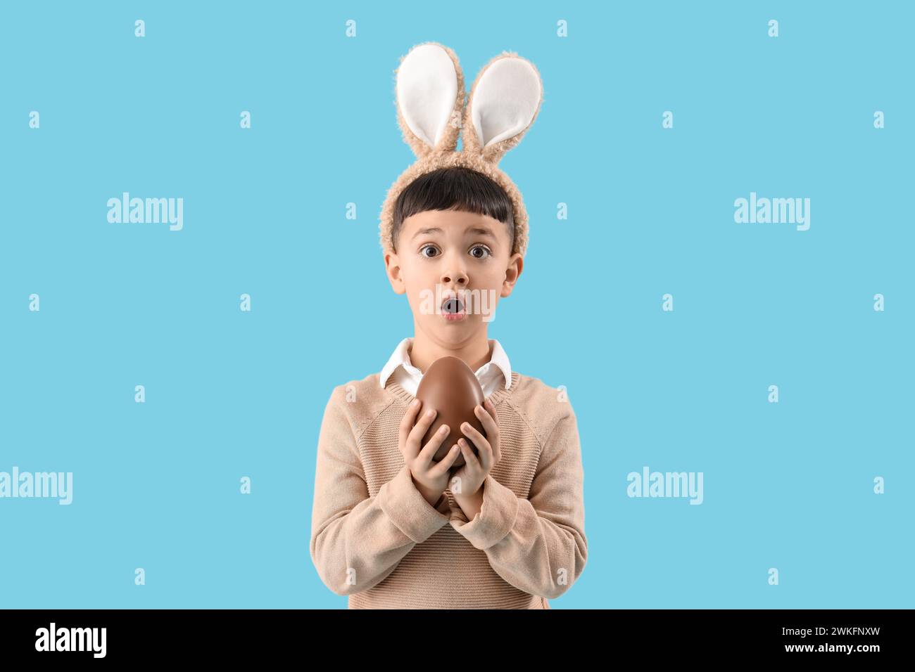 Shocked little boy wearing bunny ears with chocolate egg on blue ...
