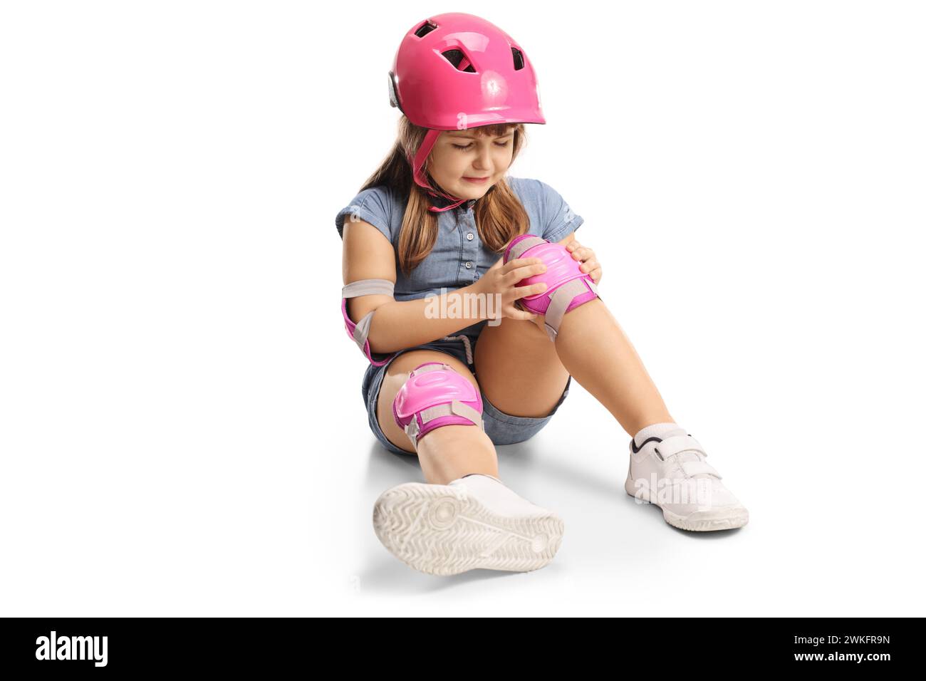 Sad little girl with pads and helmet sitting on the floor with injured ...