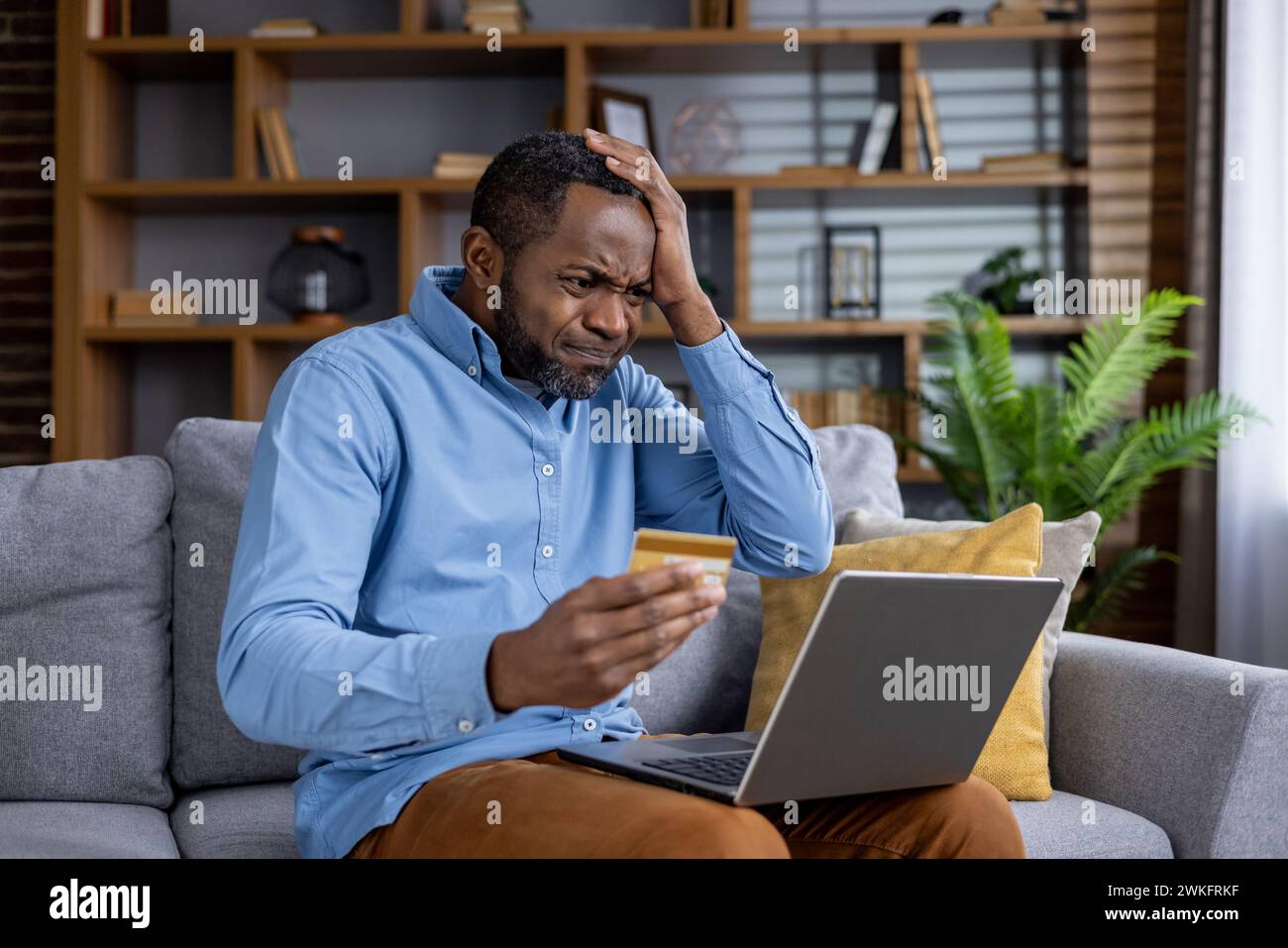 Stressed man holding credit card looking at laptop screen, showing ...