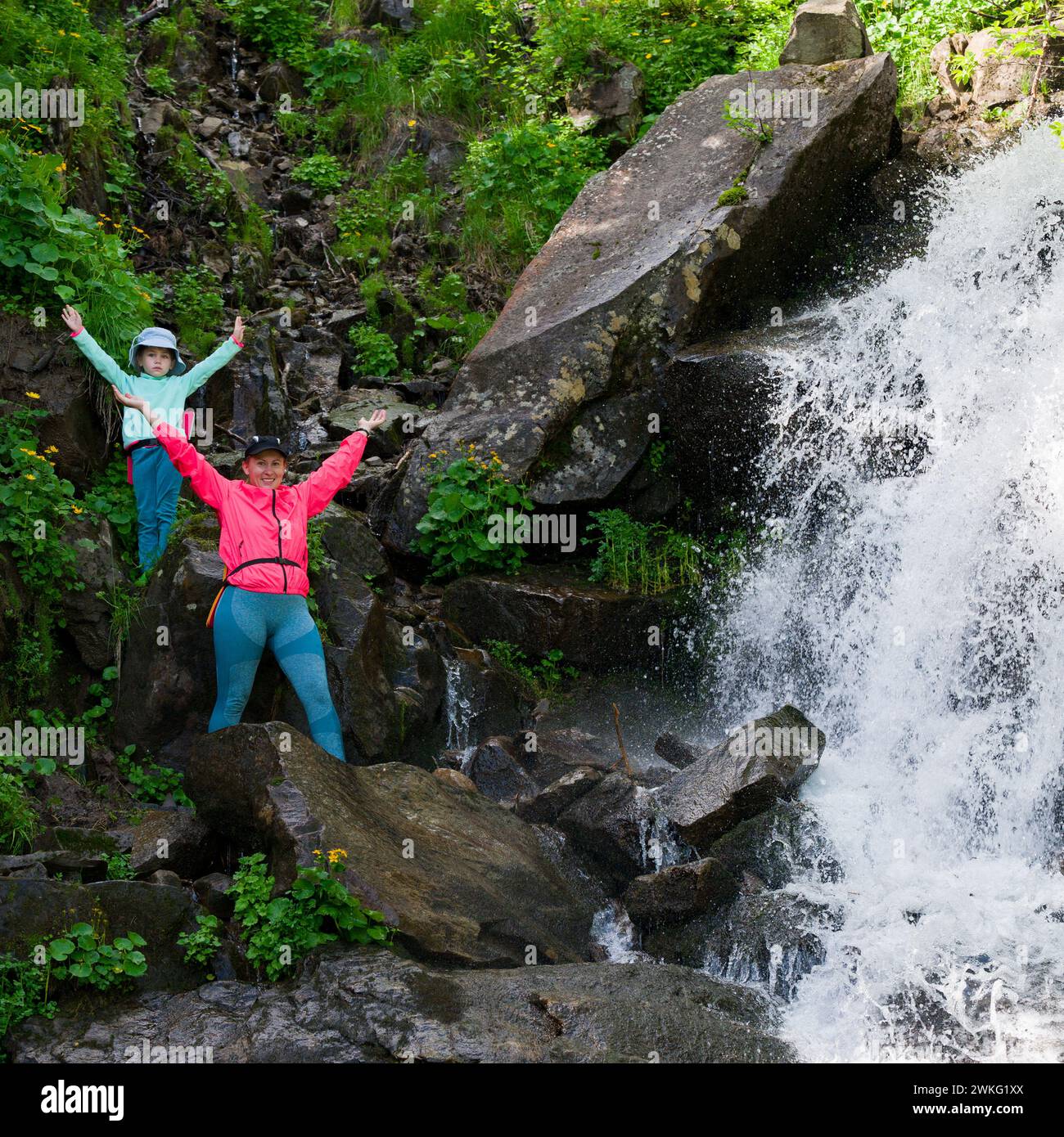Mother and daughter are standing near a mountain waterfall, active ...