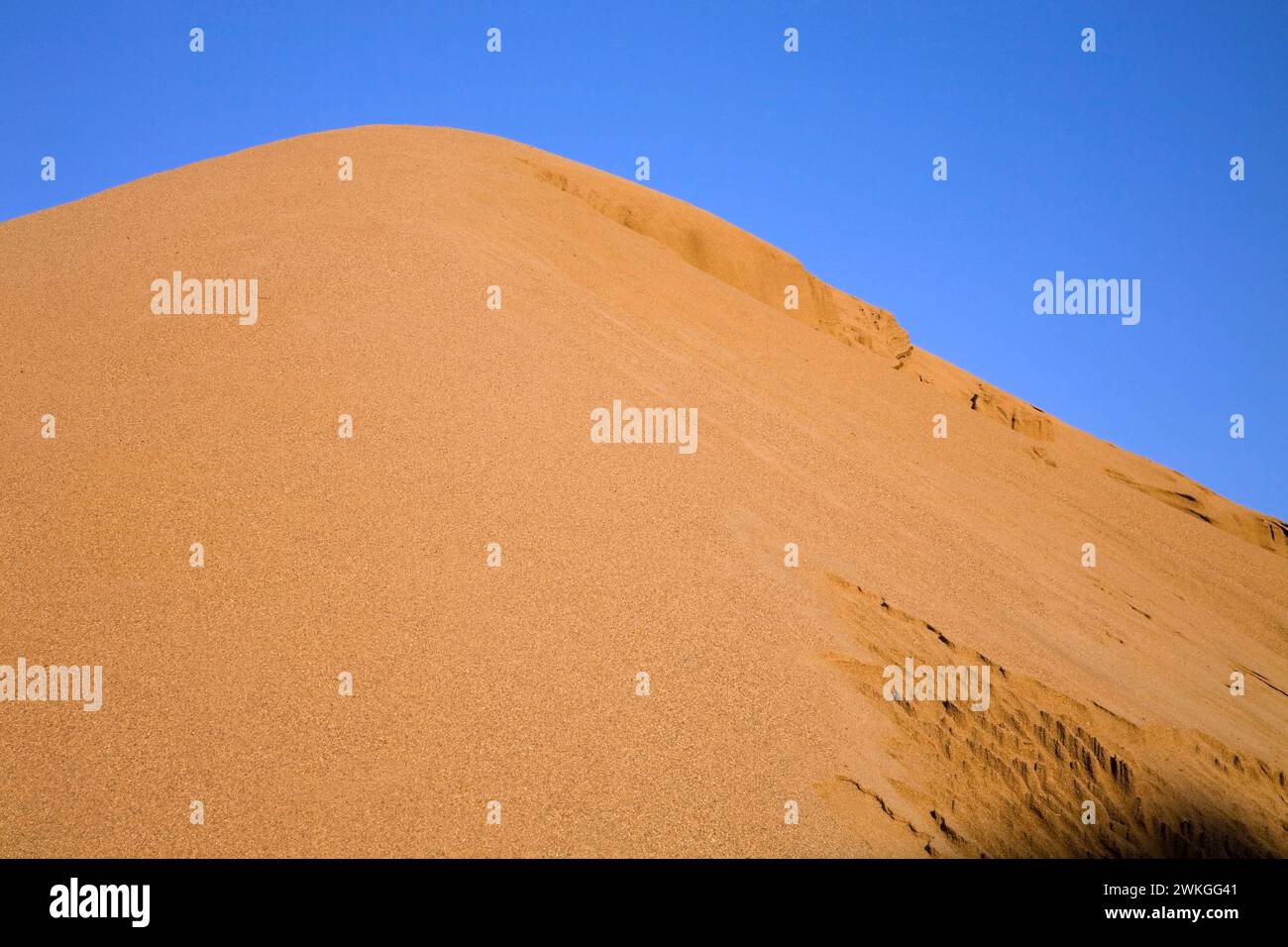 Mound of tan colored sand in commercial sandpit in late afternoon light ...