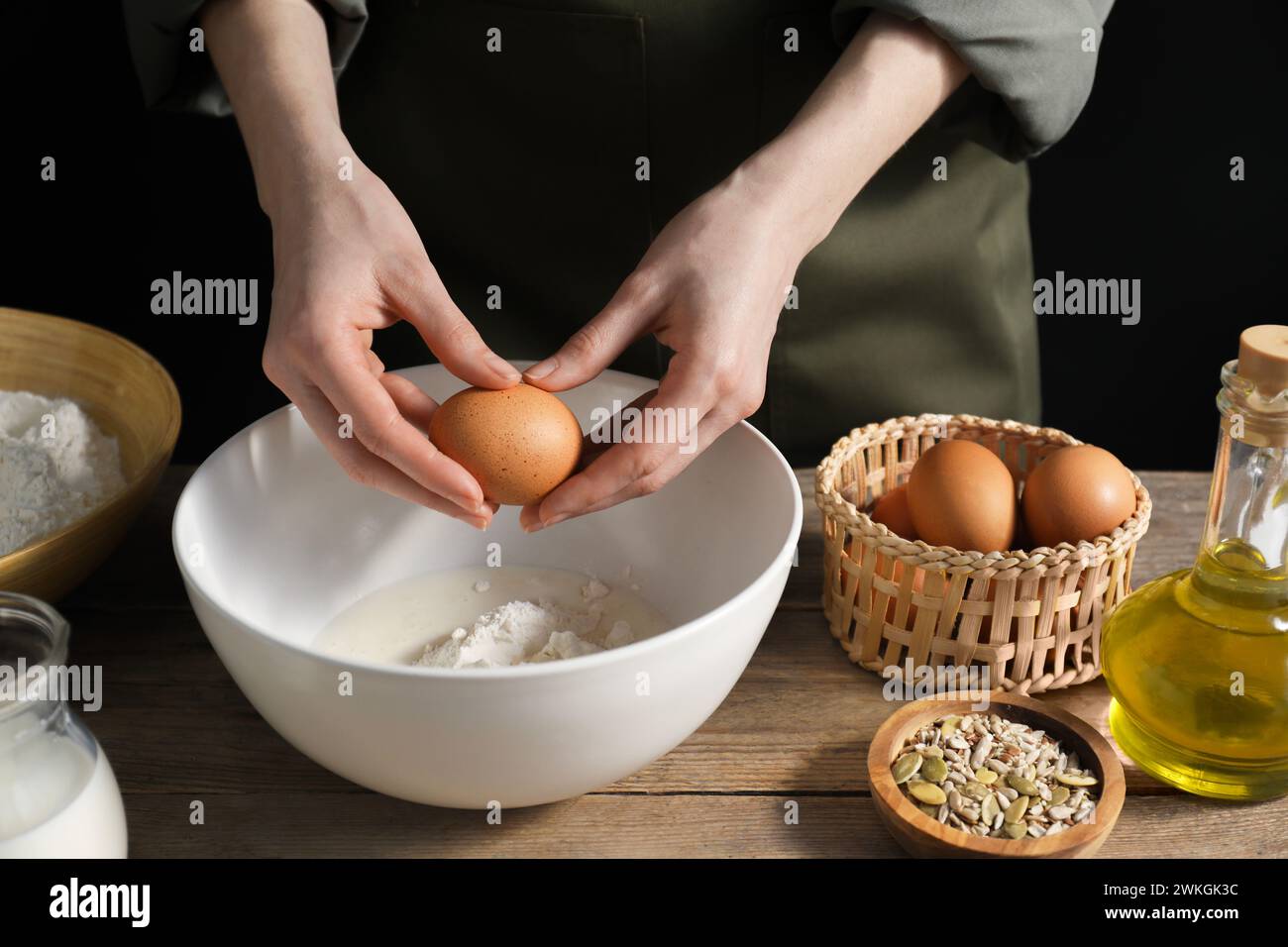 Making bread. Woman adding egg into dough at wooden table on dark background, closeup Stock ...