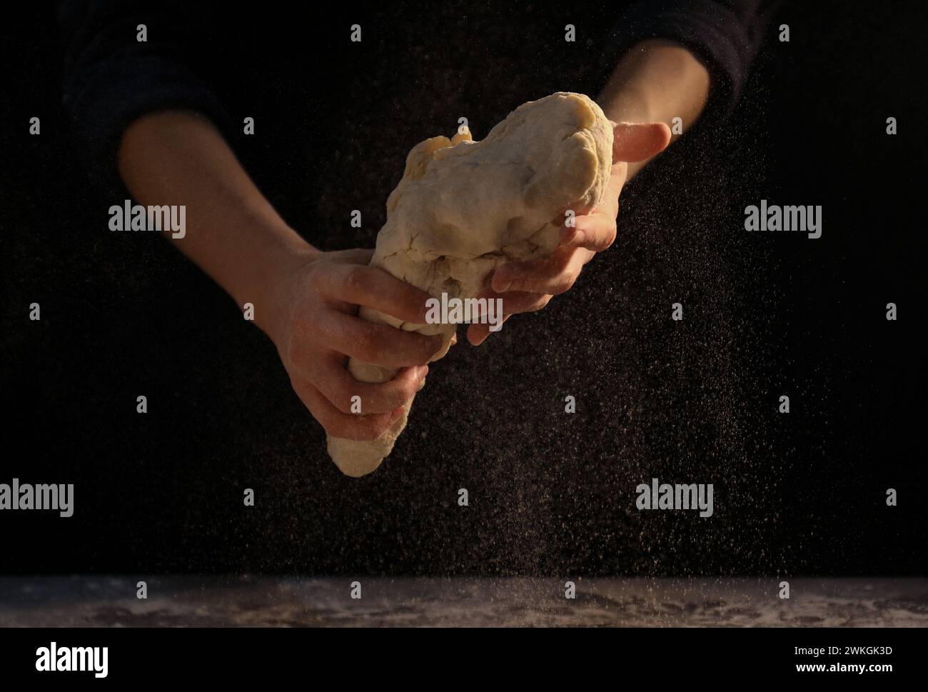 Making bread. Woman kneading dough at table on dark background, closeup ...
