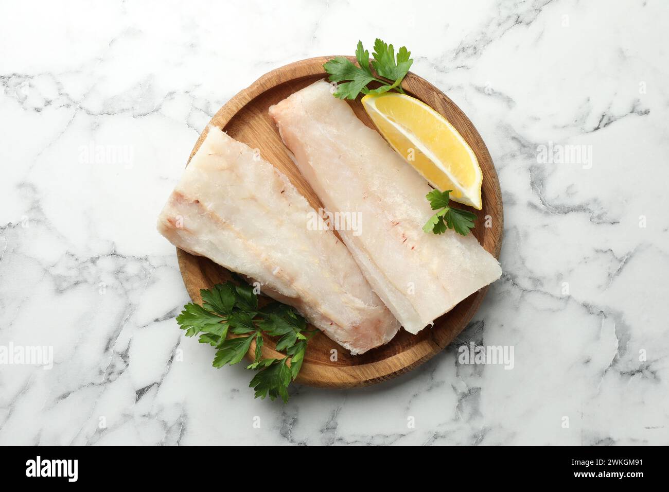 Fresh raw cod fillets with parsley and lemon on white marble table, top ...