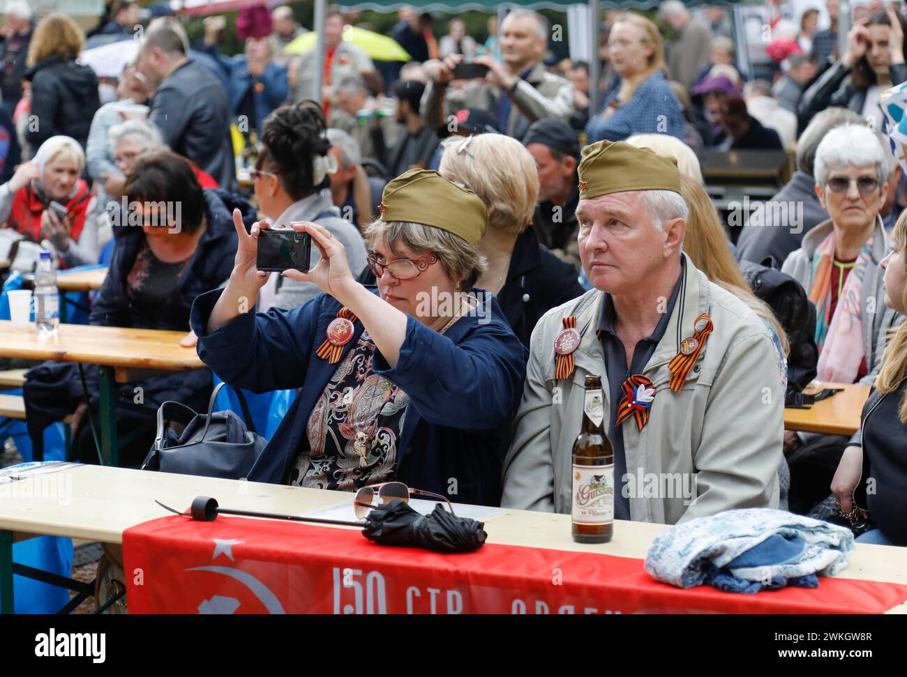 A man and a woman wear caps from Russian uniforms on the 74th ...