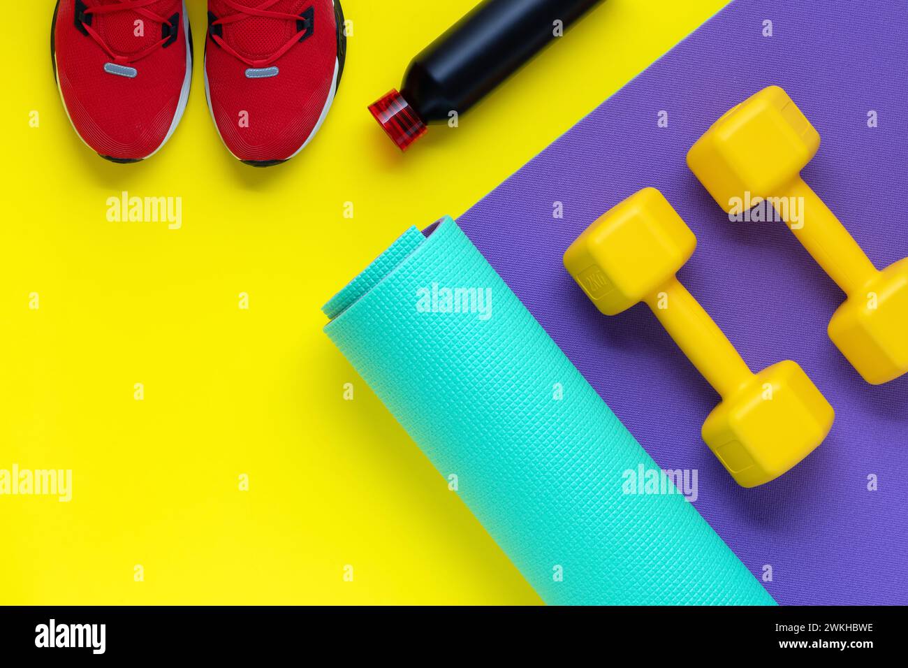 Dumbbells and sneakers for sports on roll mat, yellow background ...