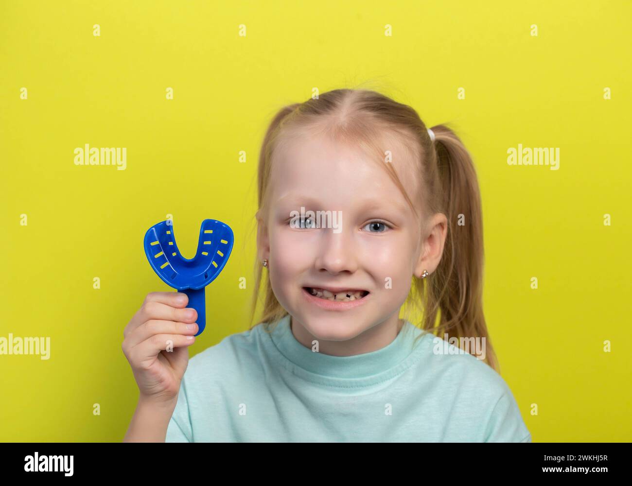 Smiling girl aged seven years old with a blue dental impression tray on ...