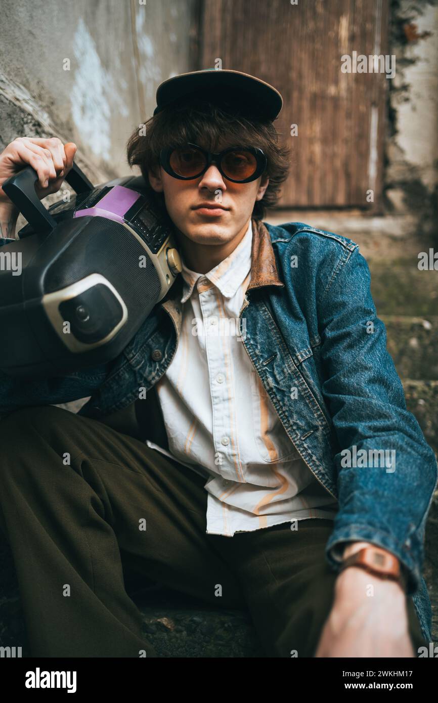 Man holding boombox on his shoulder sitting on stairs. 90s retro style ...
