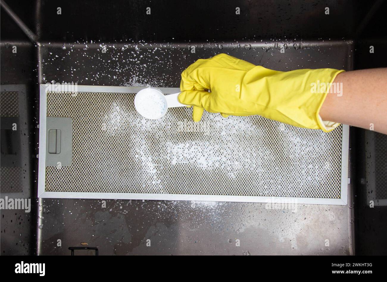 A man's hand in a yellow glove holds a spoon with oxygen bleach against ...