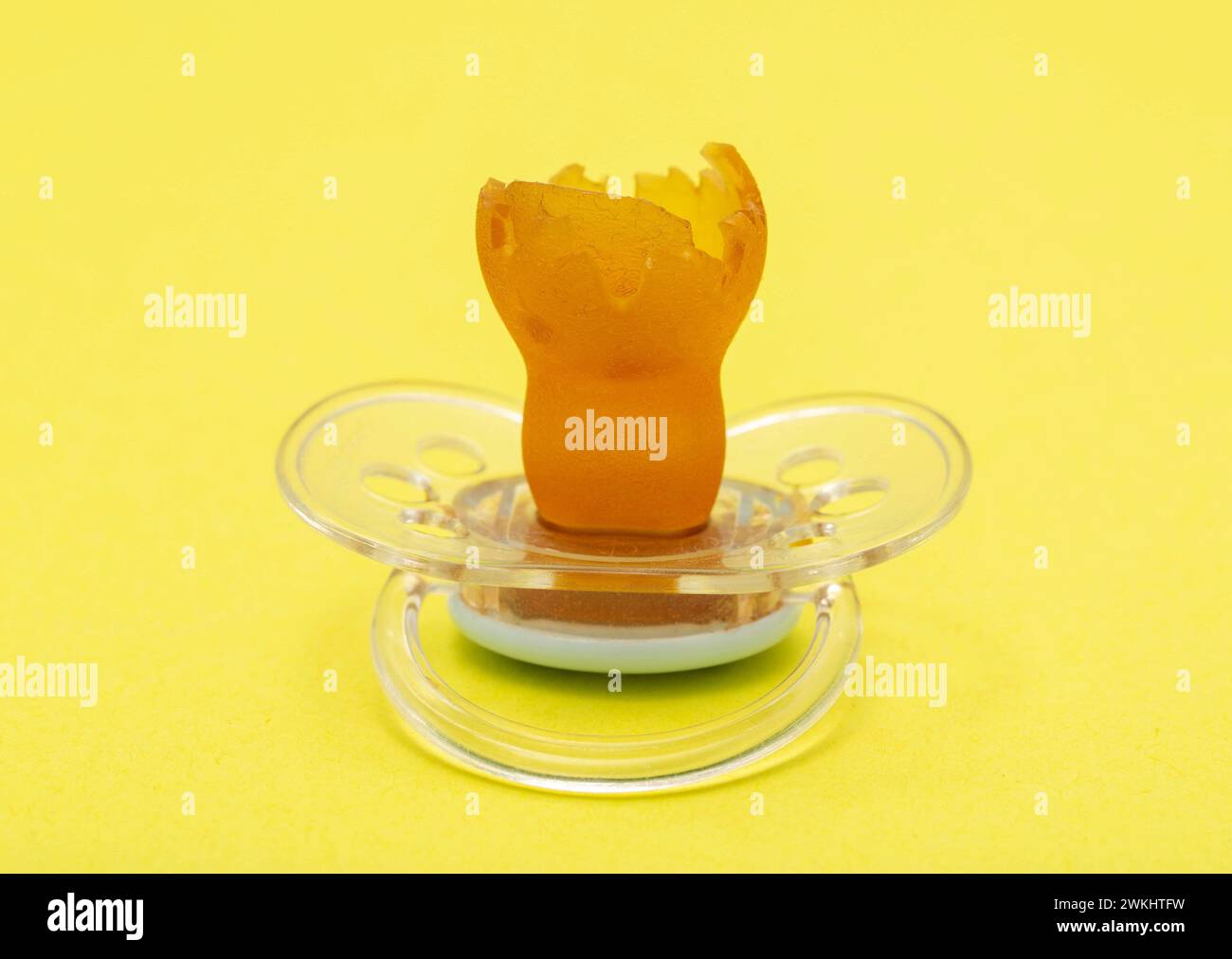 Low-quality torn baby silicone pacifier on a yellow background, close ...