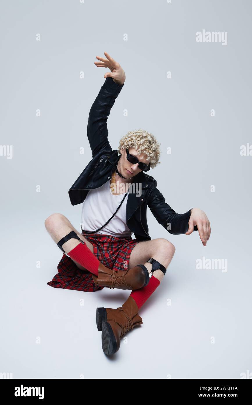 Man in leather jacket and plaid kilt seated in a dynamic dance pose ...