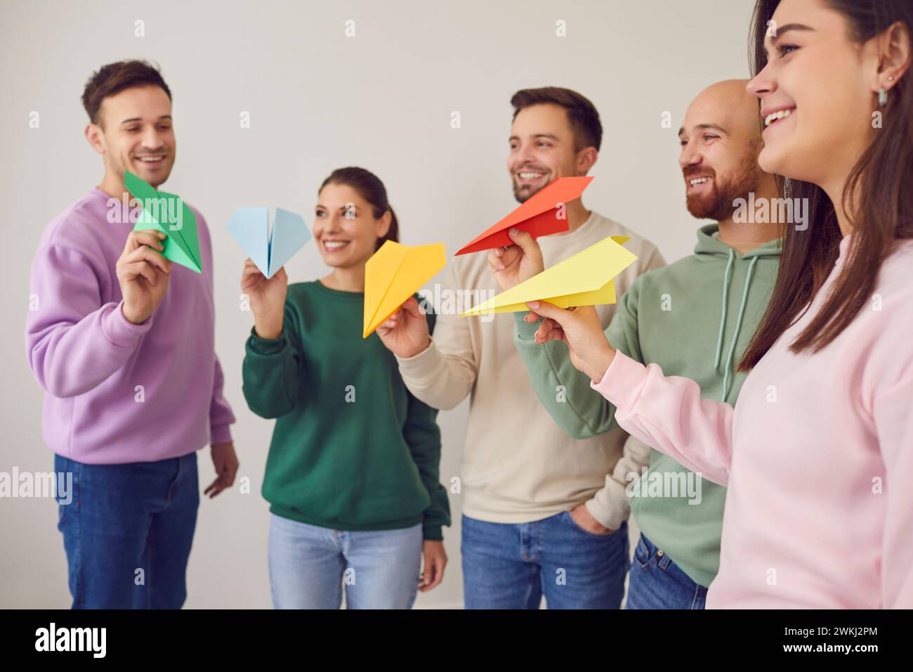 Group of happy, smiling, young people flying colorful origami airplanes ...