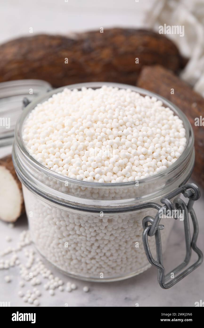 Tapioca pearls in jar and cassava roots on white table, closeup Stock ...