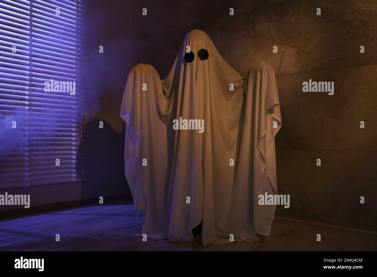 Creepy ghost. Woman covered with sheet near window in color lights ...