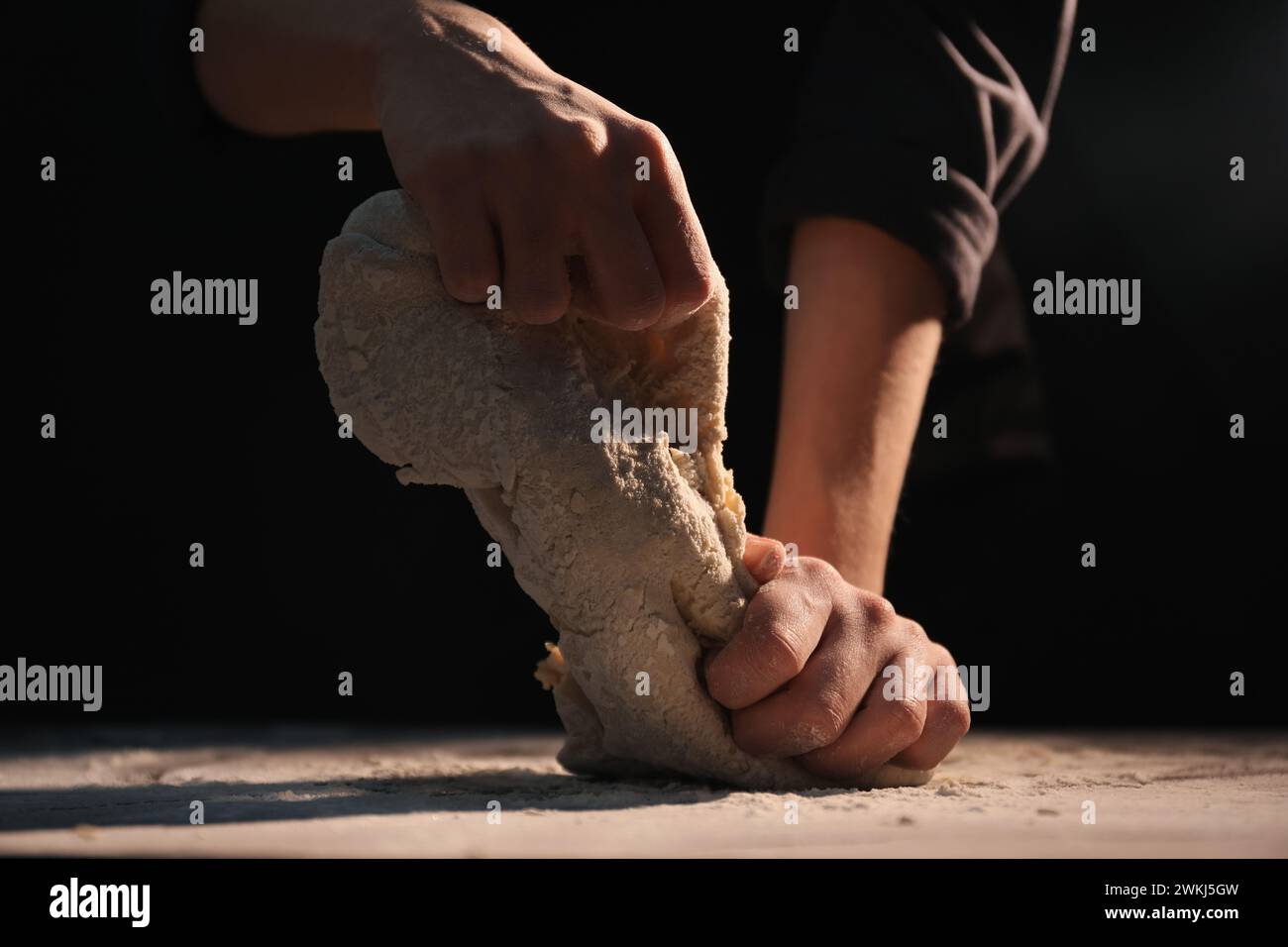 Making bread. Woman kneading dough at table on dark background, closeup ...