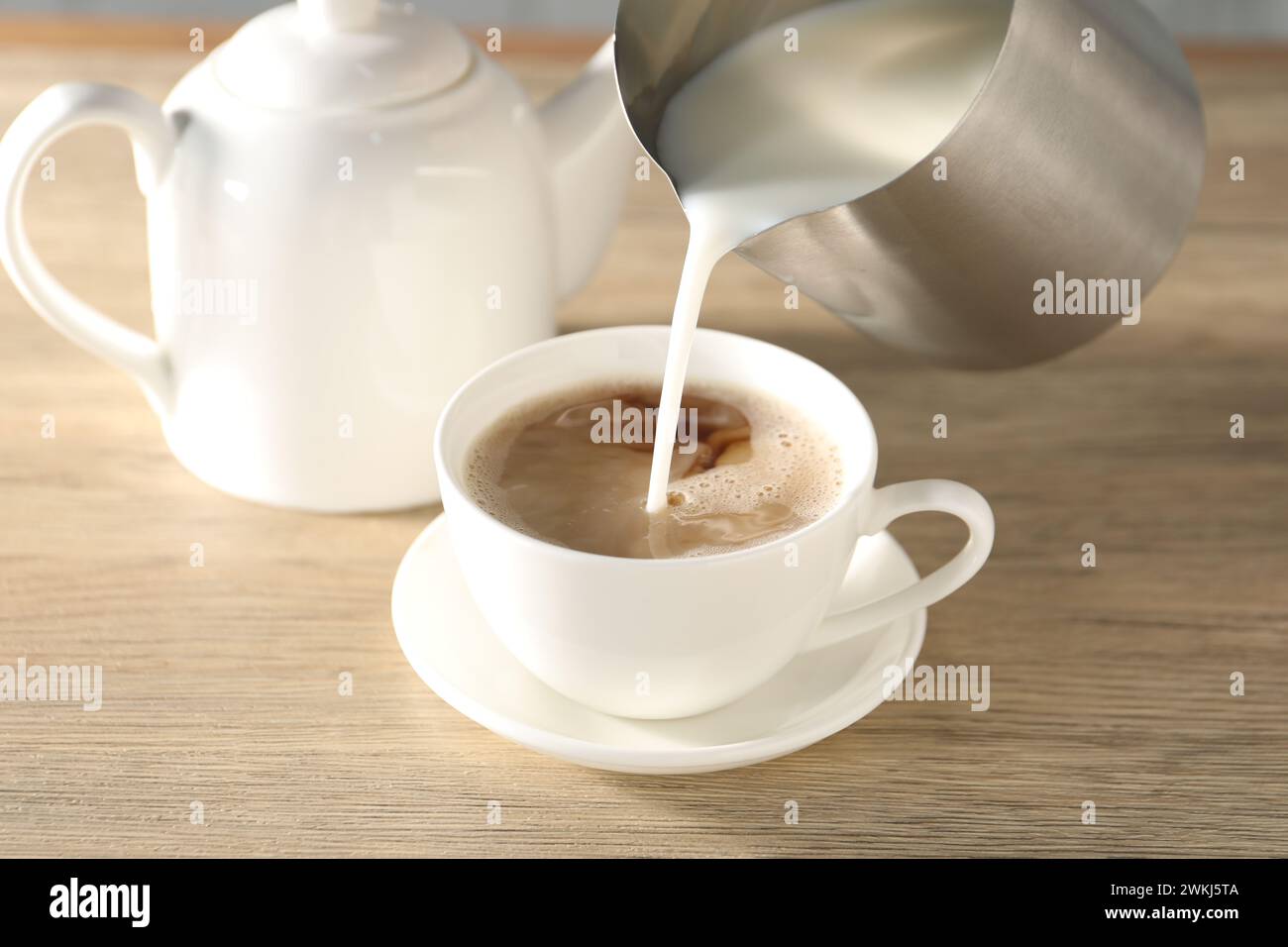 Pouring milk in tea at wooden table, closeup Stock Photo - Alamy