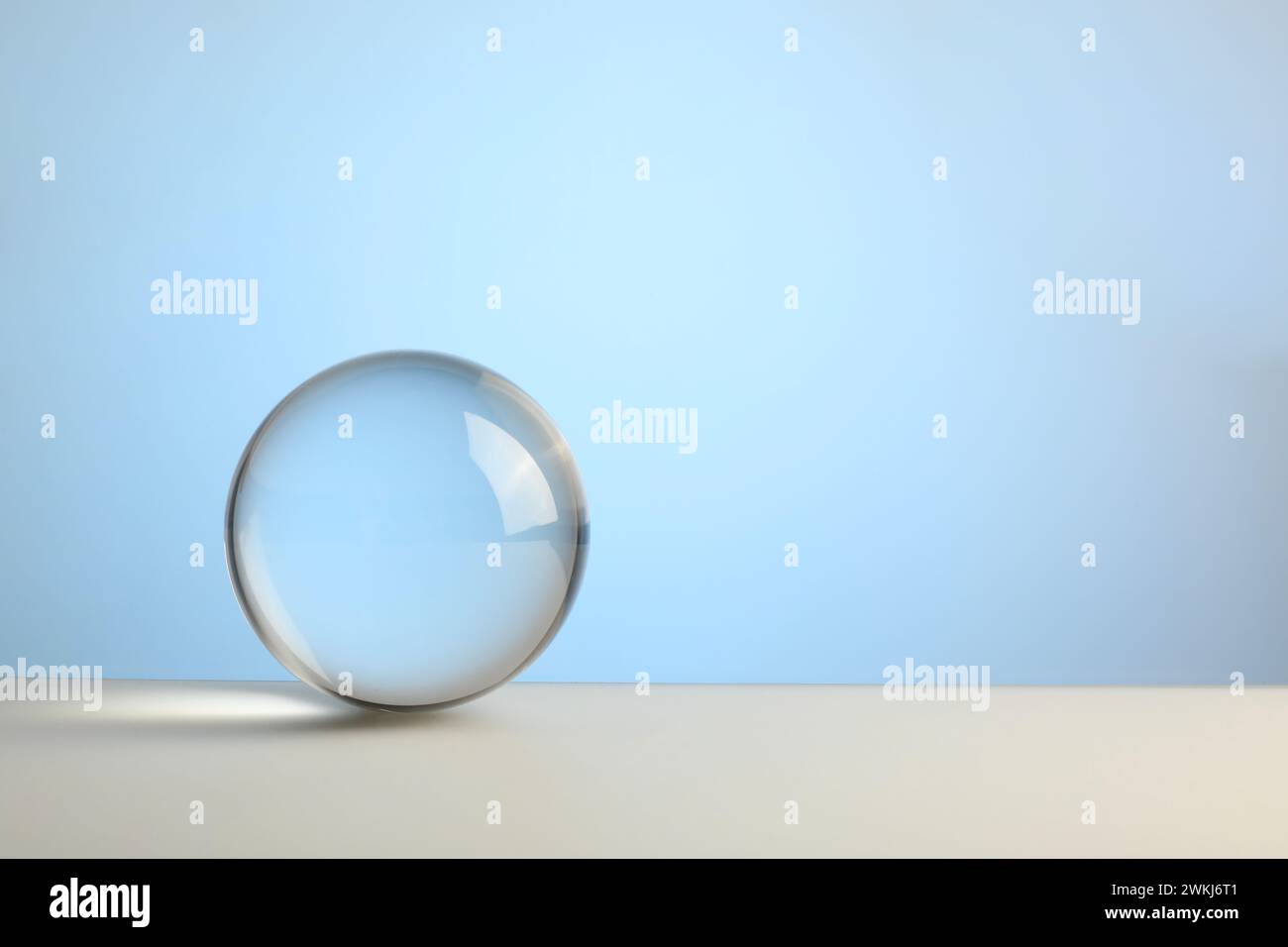 Transparent glass ball on table against light blue background. Space ...