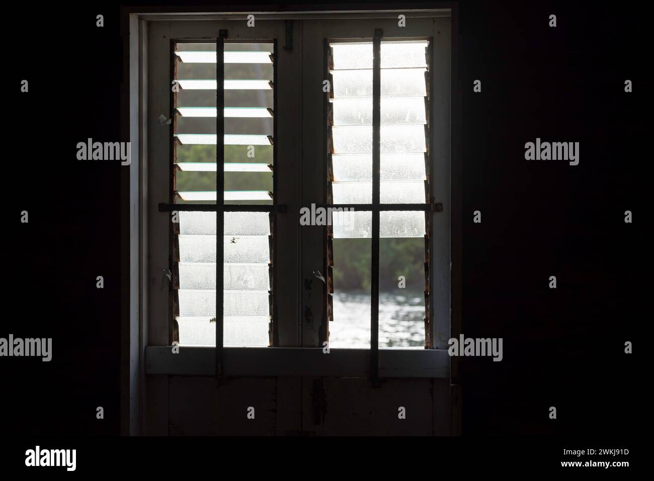 Light hitting closed frosted louvered glass windows against a jet black ...