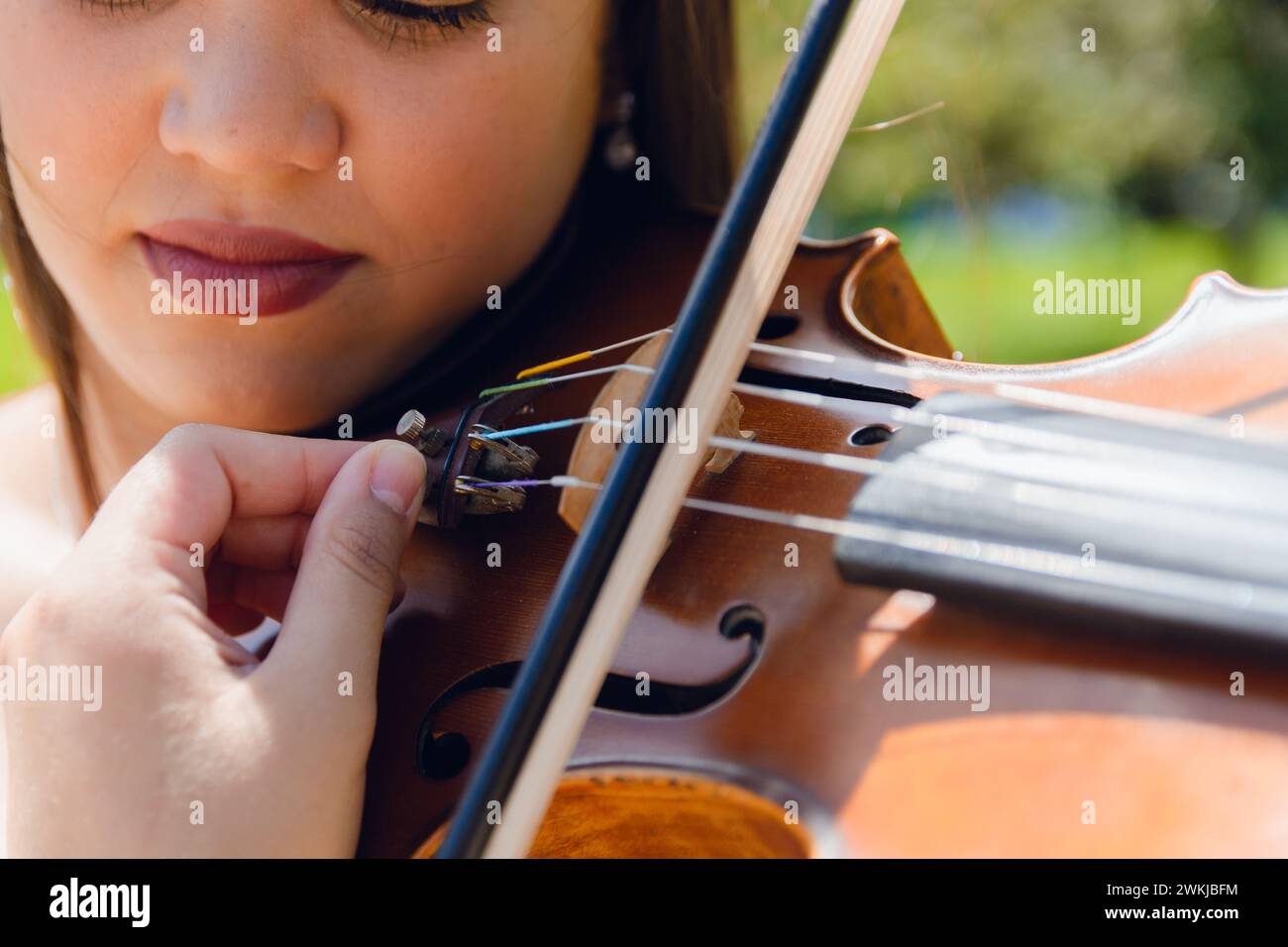 closeup of young latina busker woman violinist tuning violin outdoors before starting work as ...