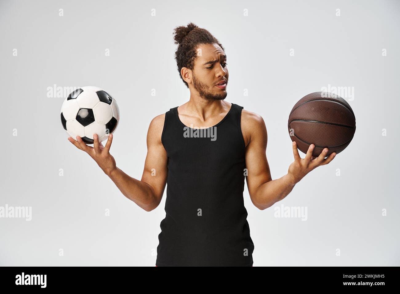 confused african american sportsman posing with football and basketball ...