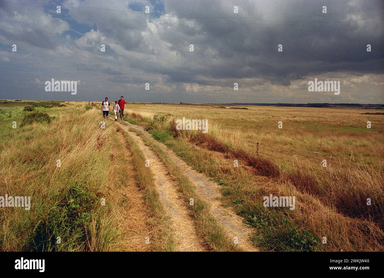 Stormy looking clouds gather over walkers on a pathway on the Blakeney ...