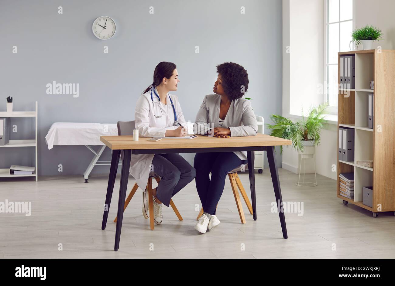 Woman doctor and her patient sitting at table and talking about medical ...