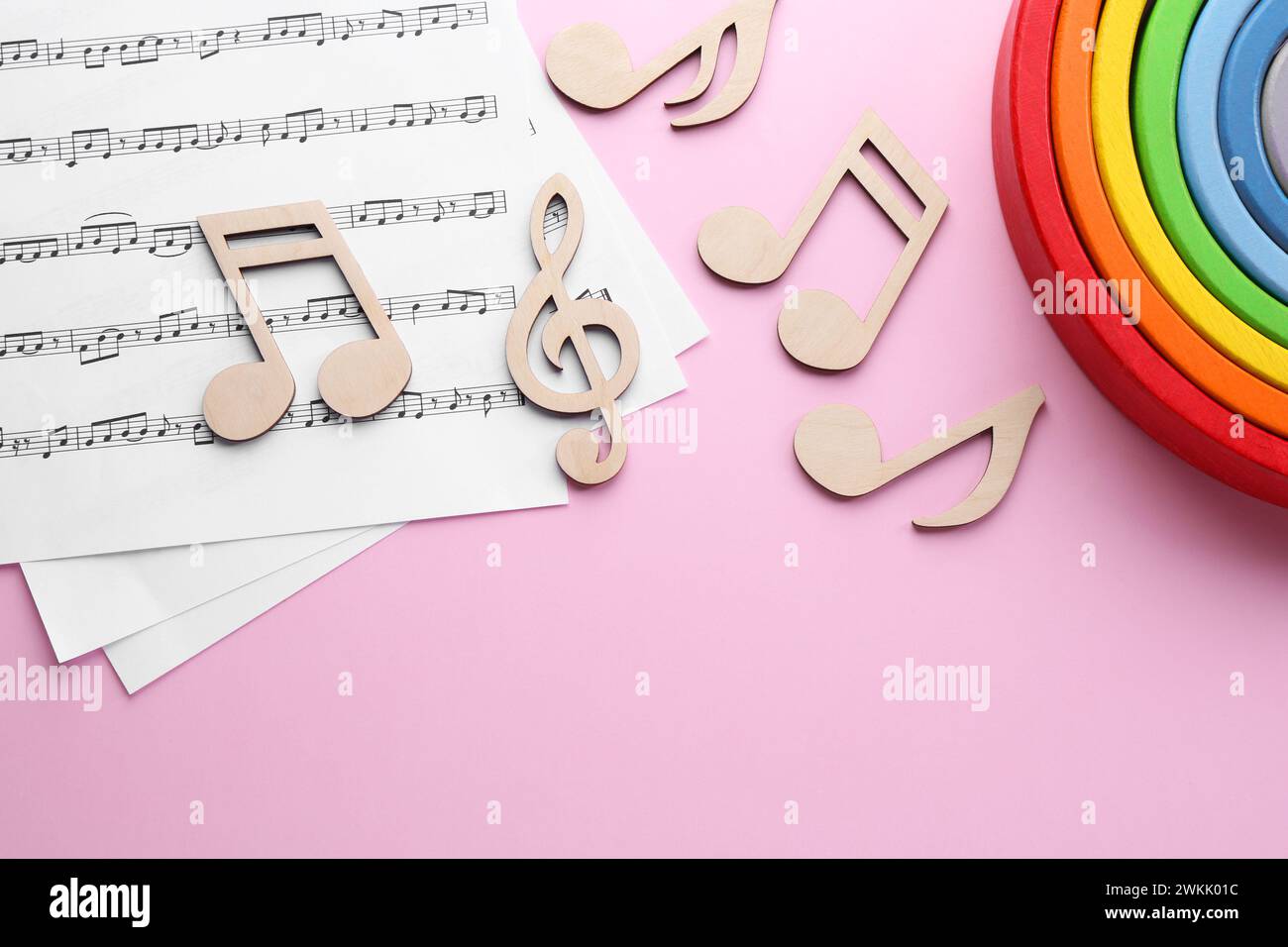 Baby songs. Music sheets, wooden notes and toy rainbow on pink ...