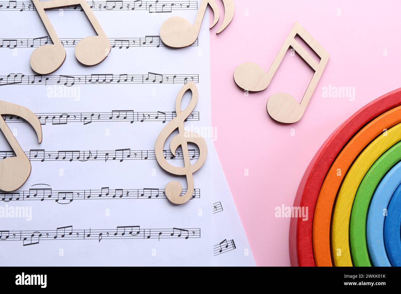 Baby songs. Music sheets, wooden notes and toy rainbow on pink ...