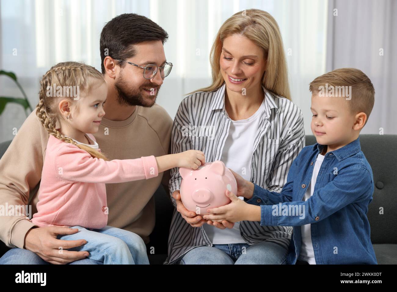 Family budget. Little girl putting coin into piggy bank while her ...