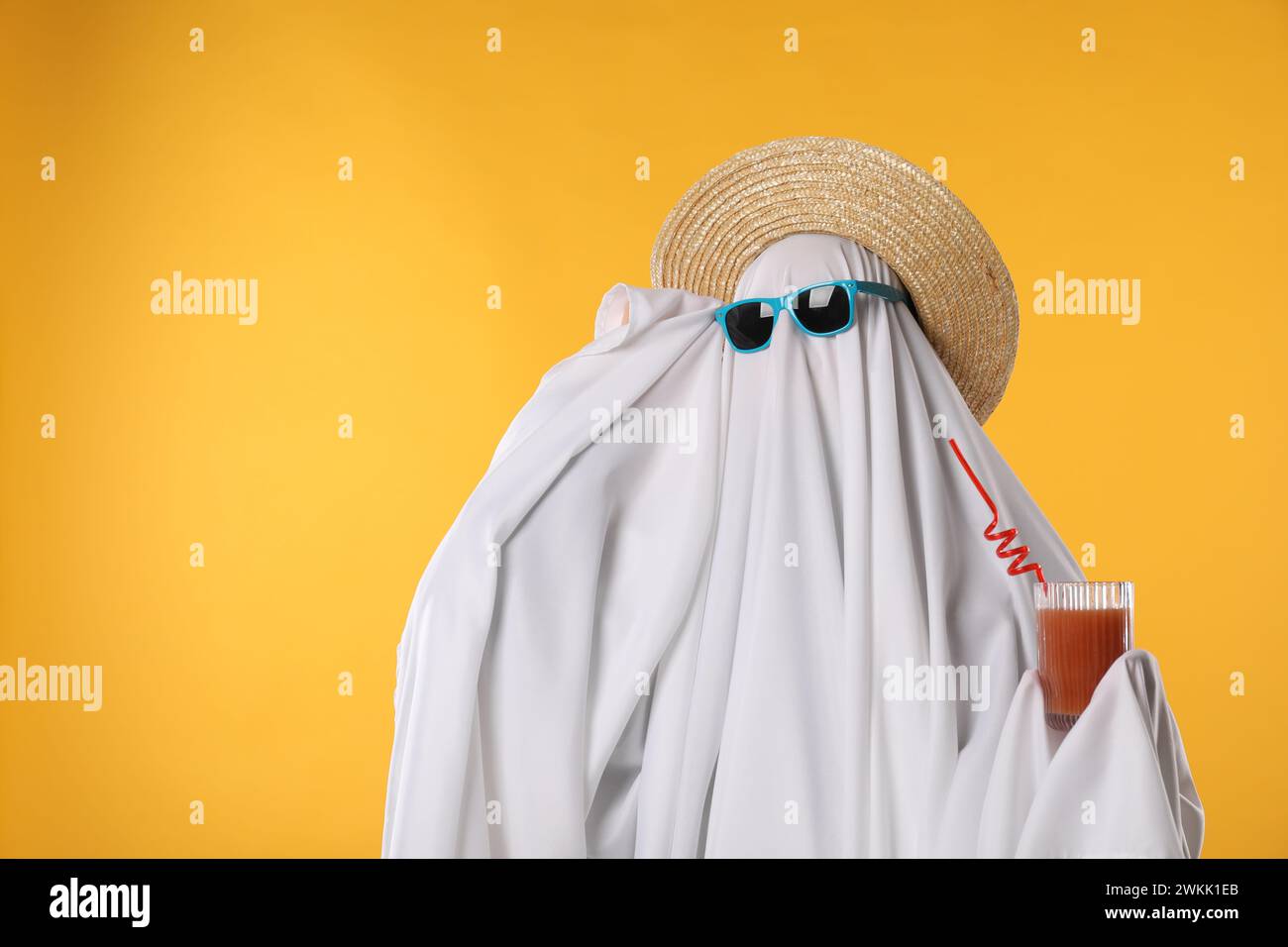 Person in ghost costume, sunglasses and straw hat holding glass of ...