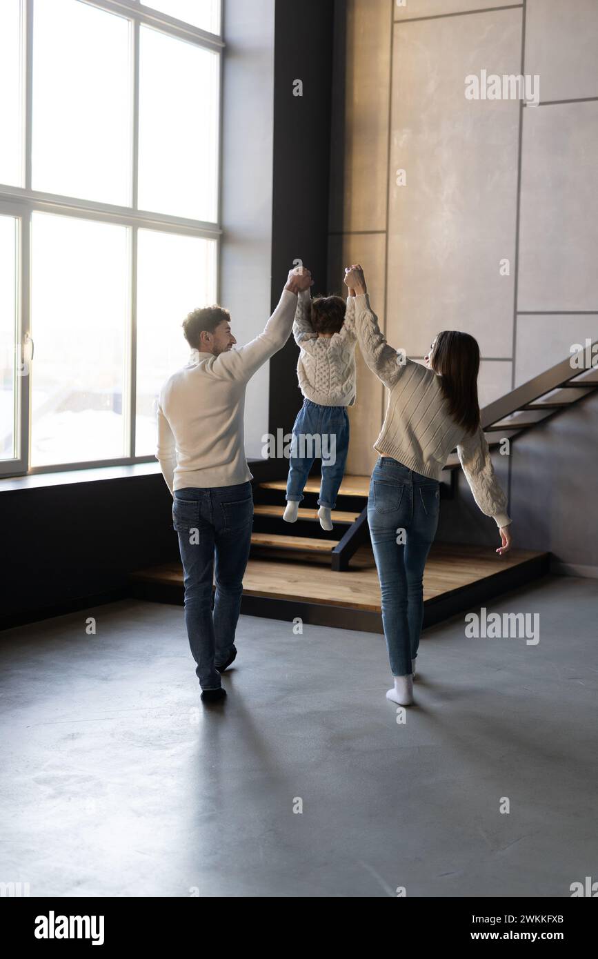 Full body father and mother smiling and lifting son near couch in ...