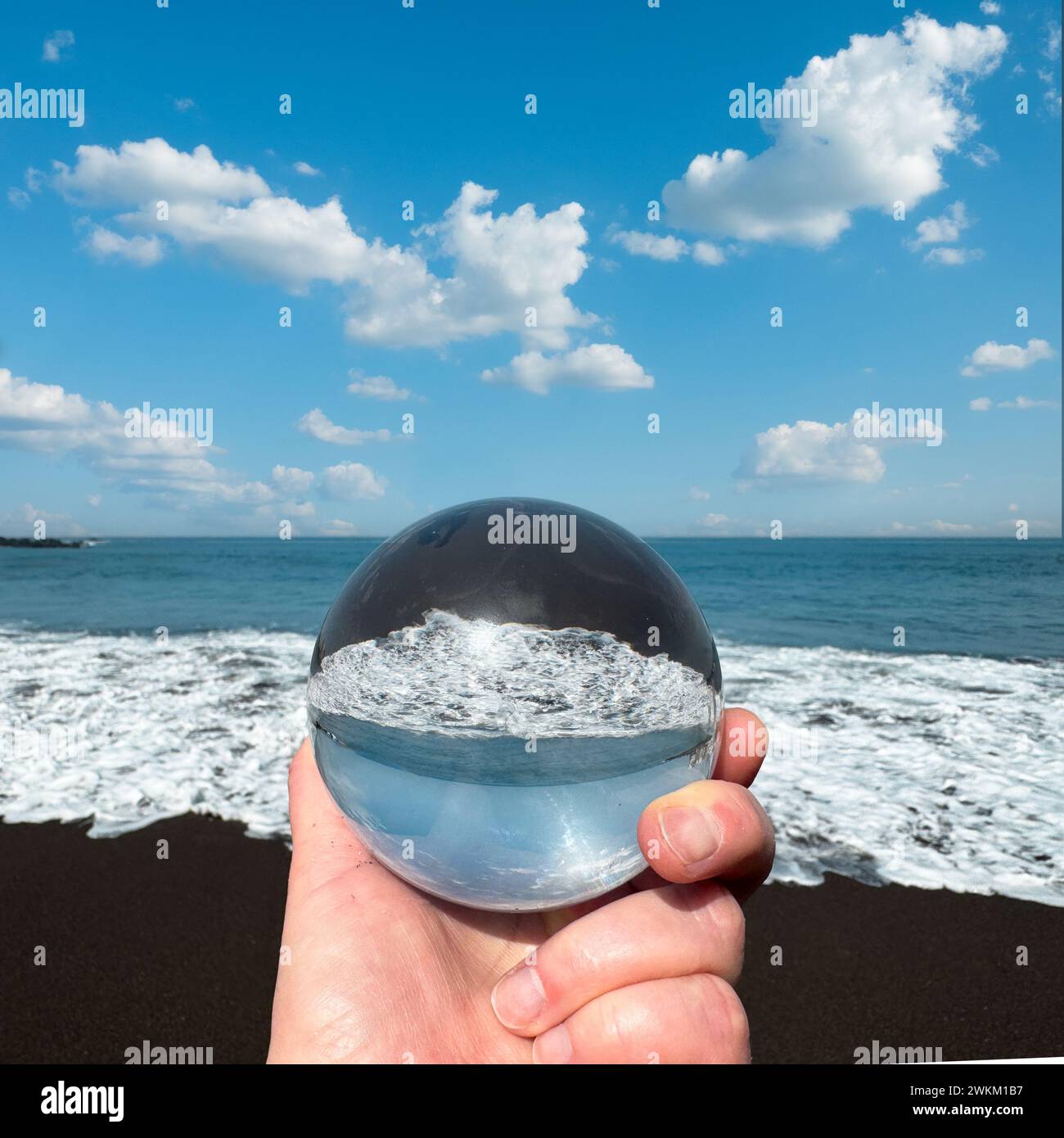 Close-up on a hand holding glass crystal ball on volcanic seaside ...