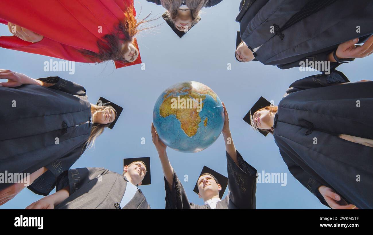 College graduates stand in a circle and hold a geographical globe of ...