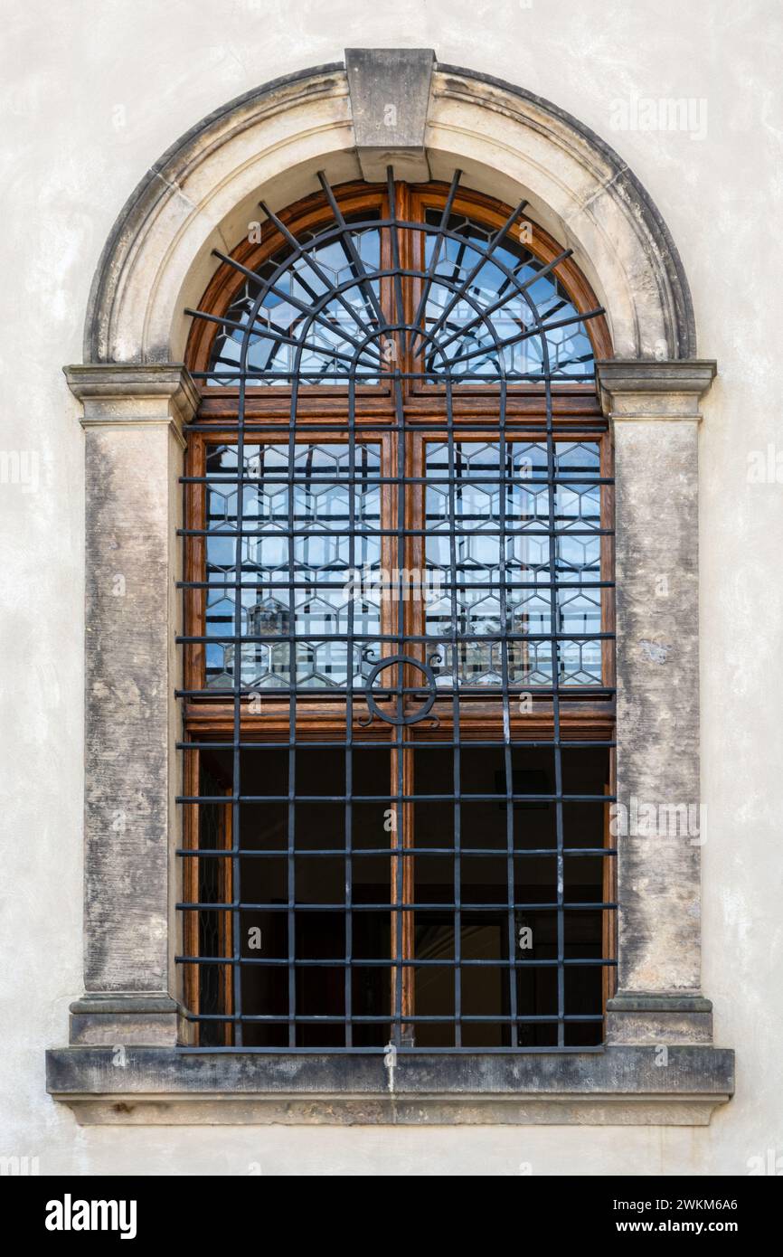 Arched window with a forged metal grill against a wall of beige stone ...