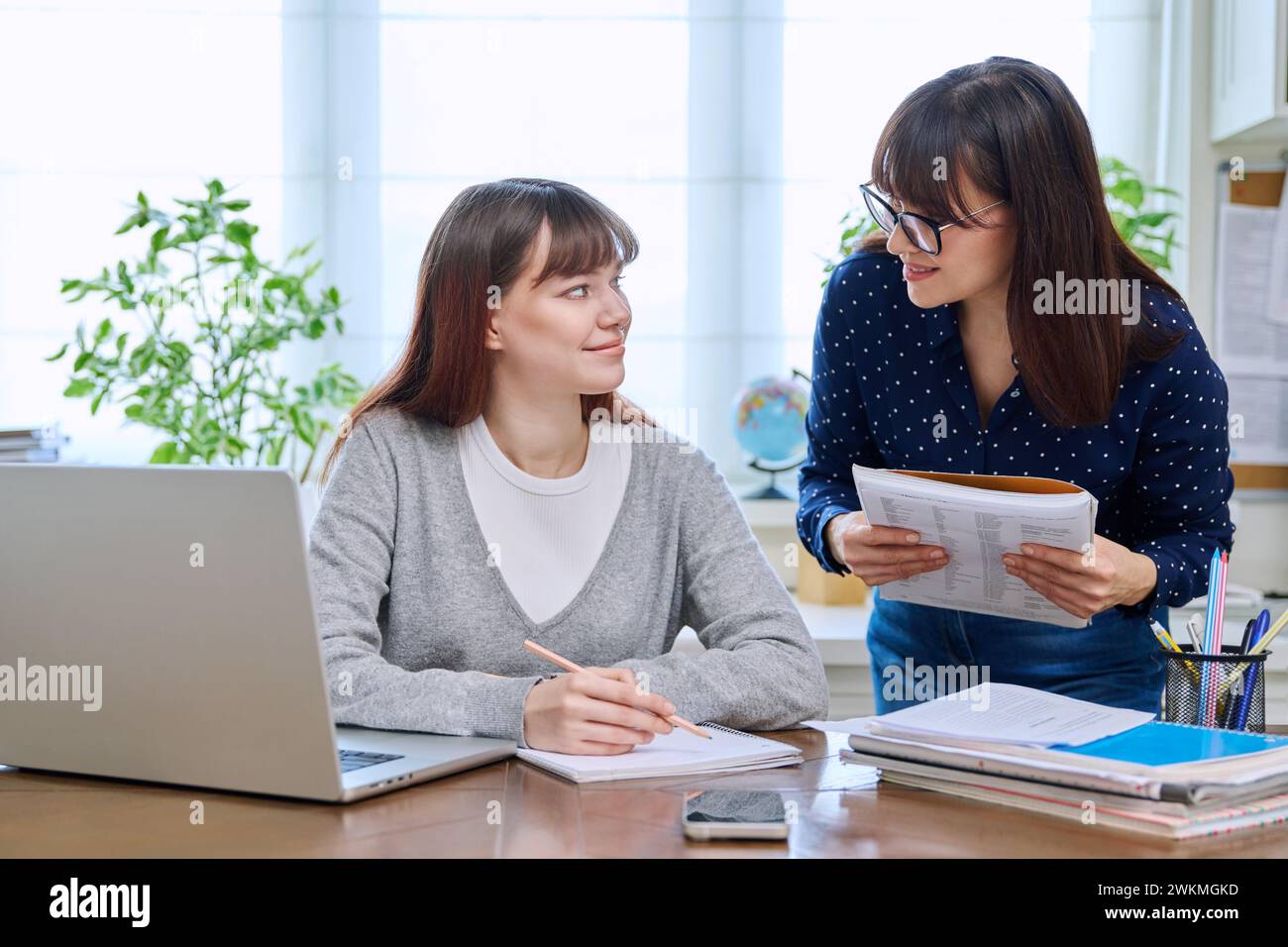 Teenage student studying at desk with computer, trainer mentor helping ...