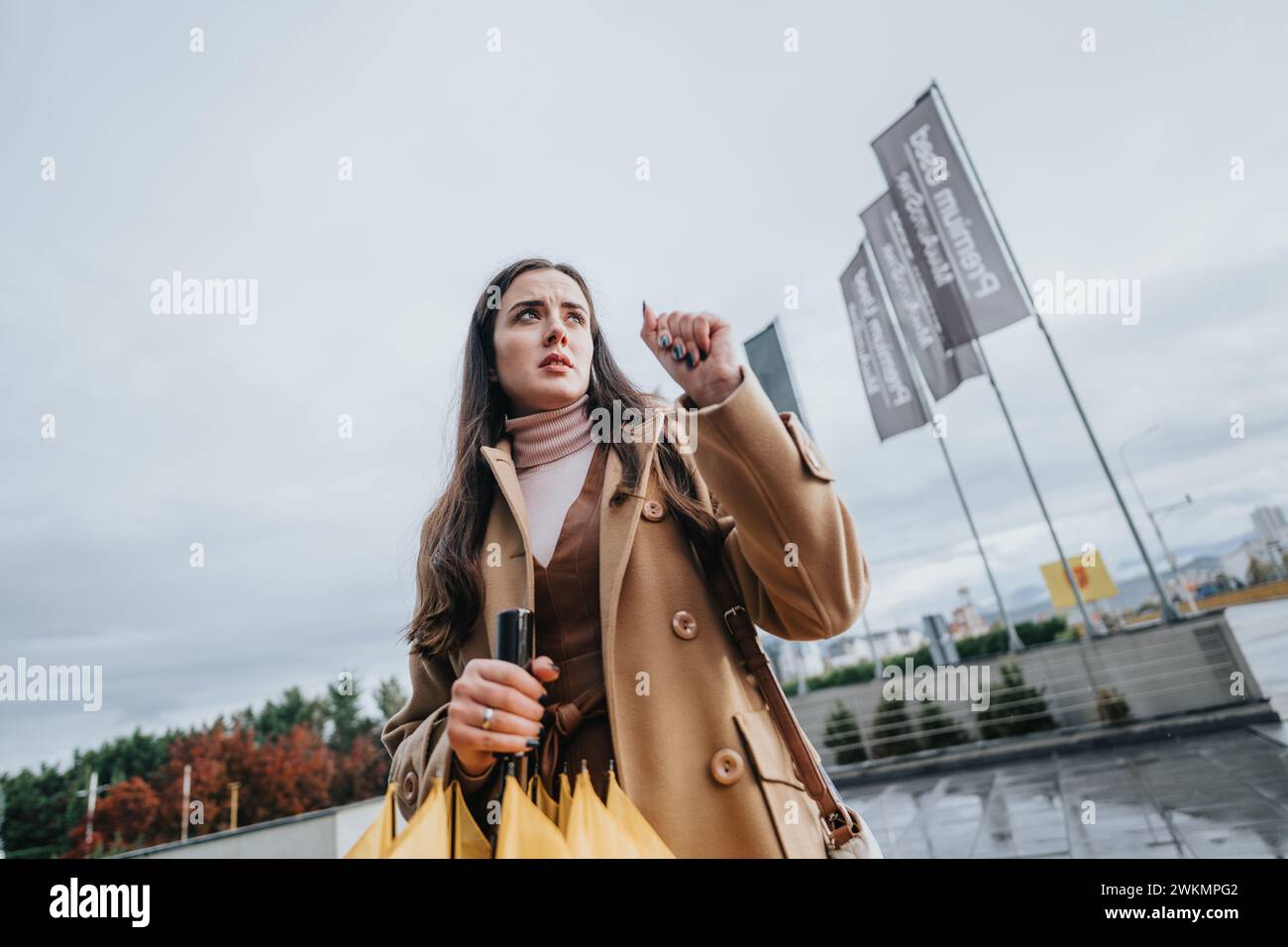 A worried young woman looks skyward, holding an umbrella and shopping ...