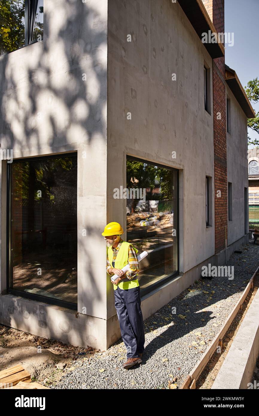 good looking dedicated cottage builder in safety gear with blueprint ...