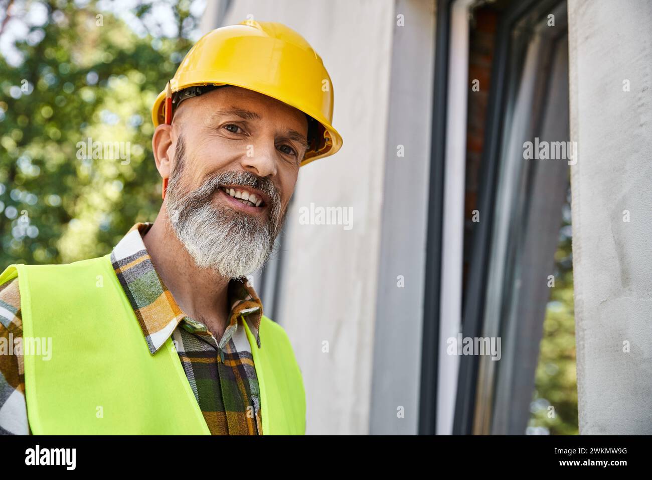 cheerful good looking cottage builder in vibrant safety vest and helmet ...