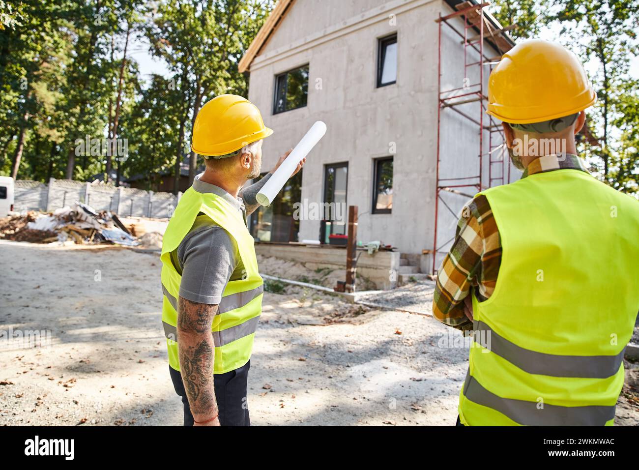 back view of devoted cottage builders in safety helmets with blueprint ...