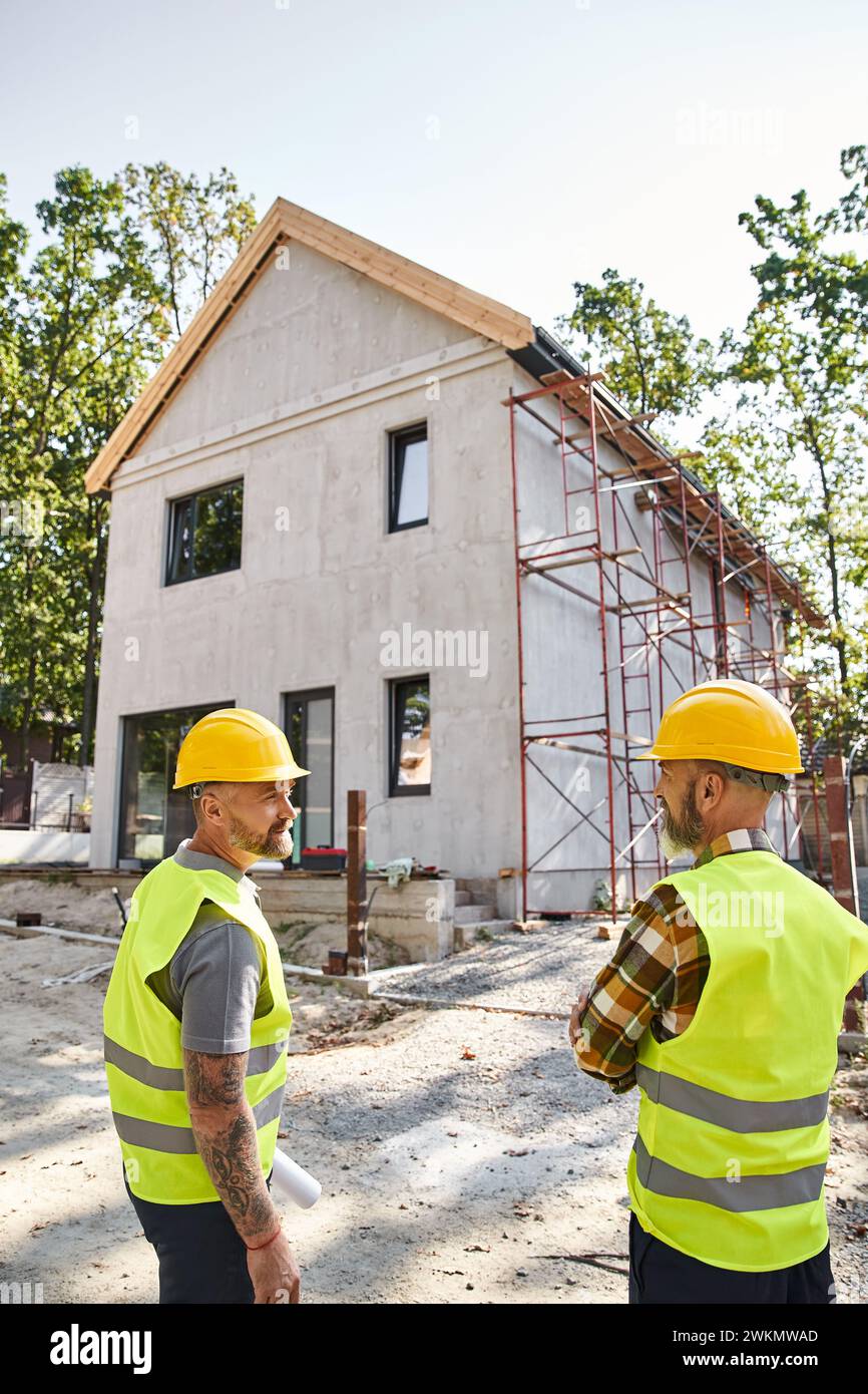 good looking devoted cottage builders in safety helmets with blueprint ...