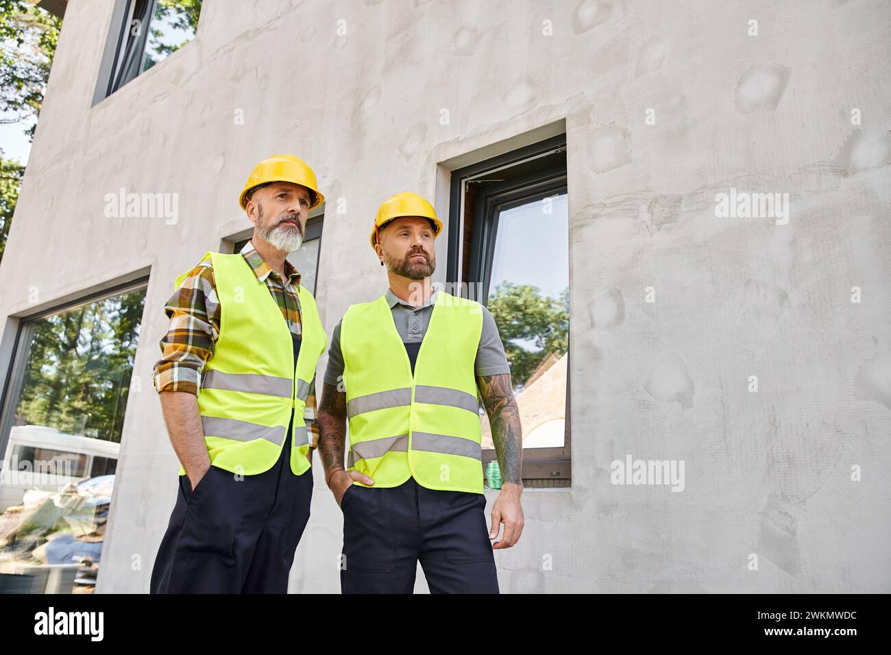 appealing devoted builders in safety helmets and vests posing outside ...