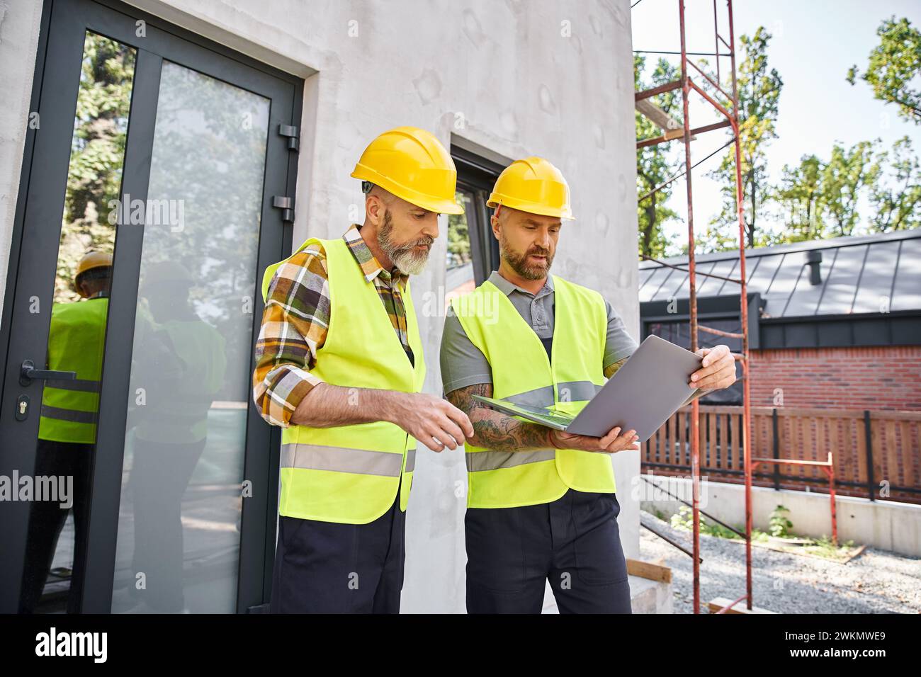 handsome bearded men in safety vests and helmets working with laptop on ...